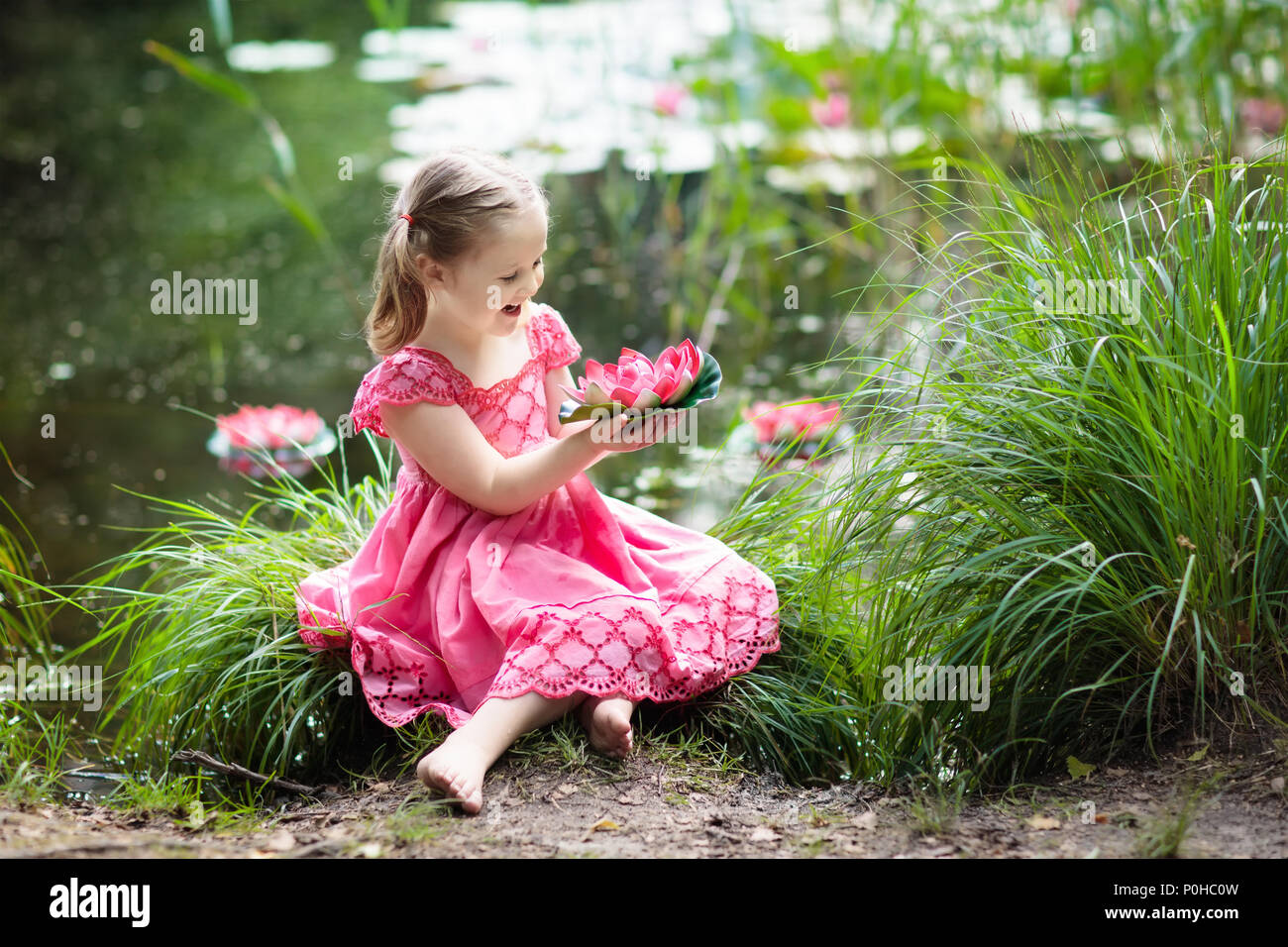 Child sitting at lake shore watching water lily flowers. Little girl ...