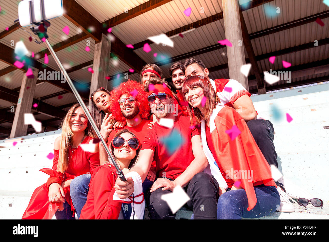 group of fans dressed in red color takes a selfie in the stands of a ...