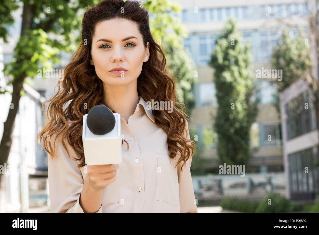 attractive serious female journalist taking interview with microphone ...