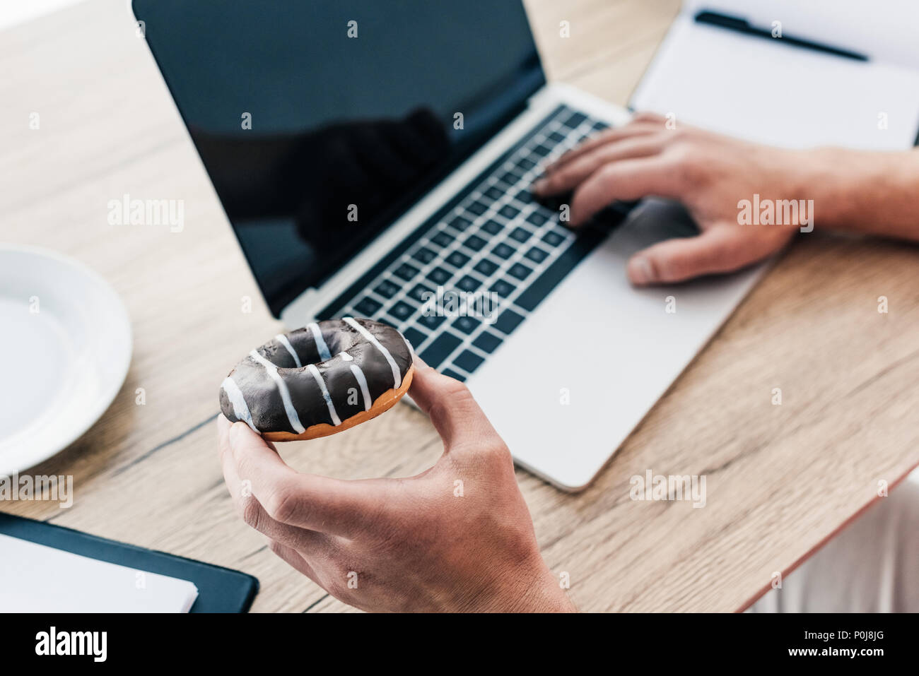 partial view of man holding doughnut and using laptop at table with ...