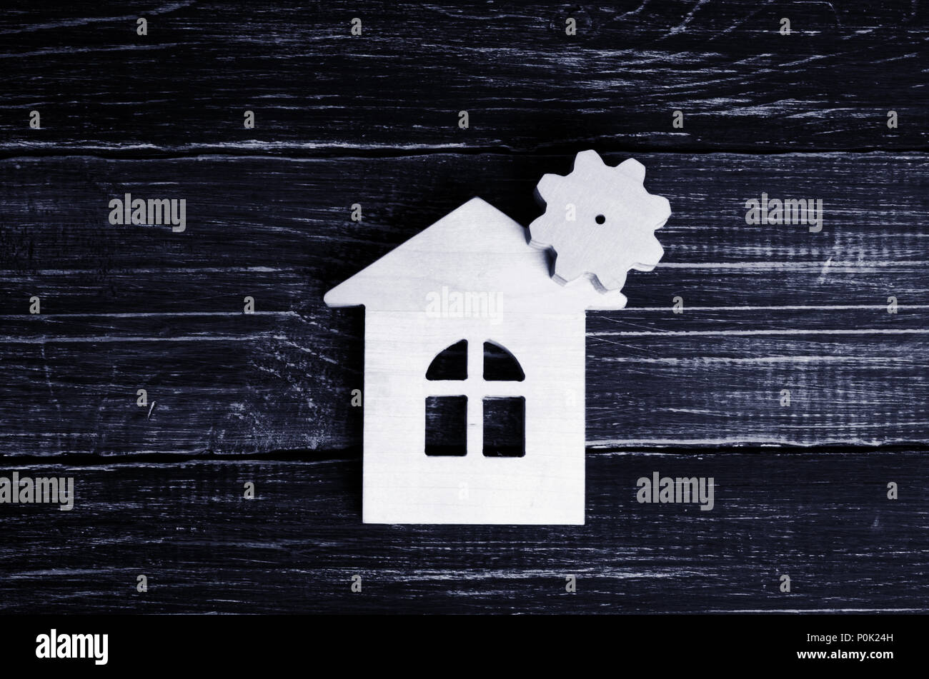 Wooden house with a gear on a background of dark wood. The concept of ...