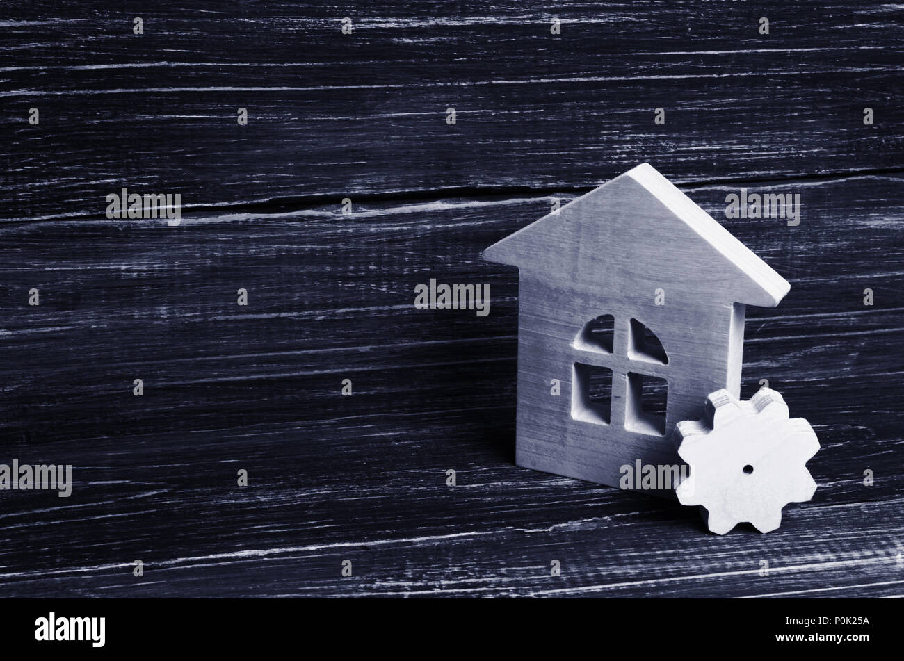 Wooden house with a gear on a background of dark wood. The concept of ...