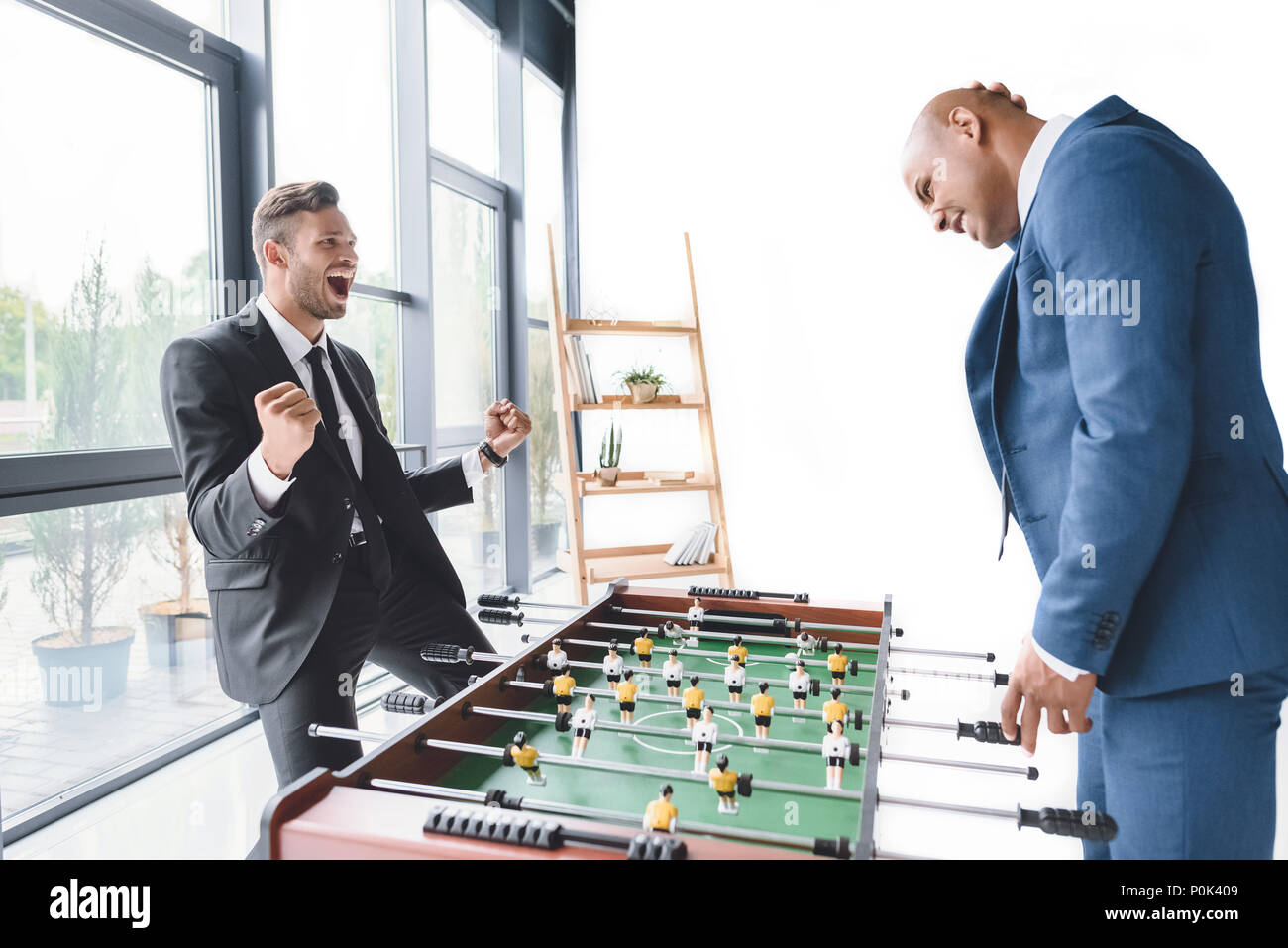 excited businessman playing table football with coworker in office ...