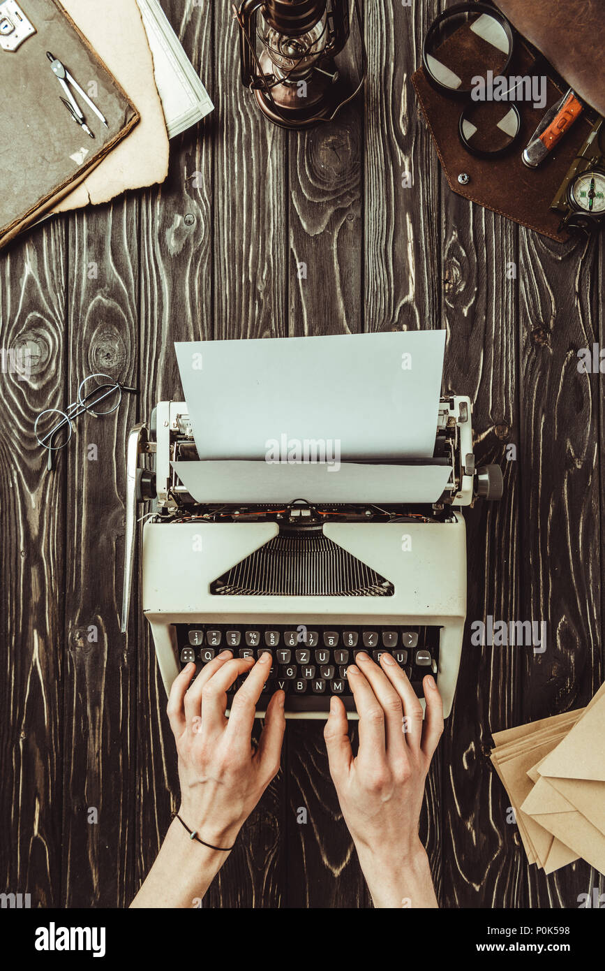 partial view of writer typing on typing machine with blank envelopes ...