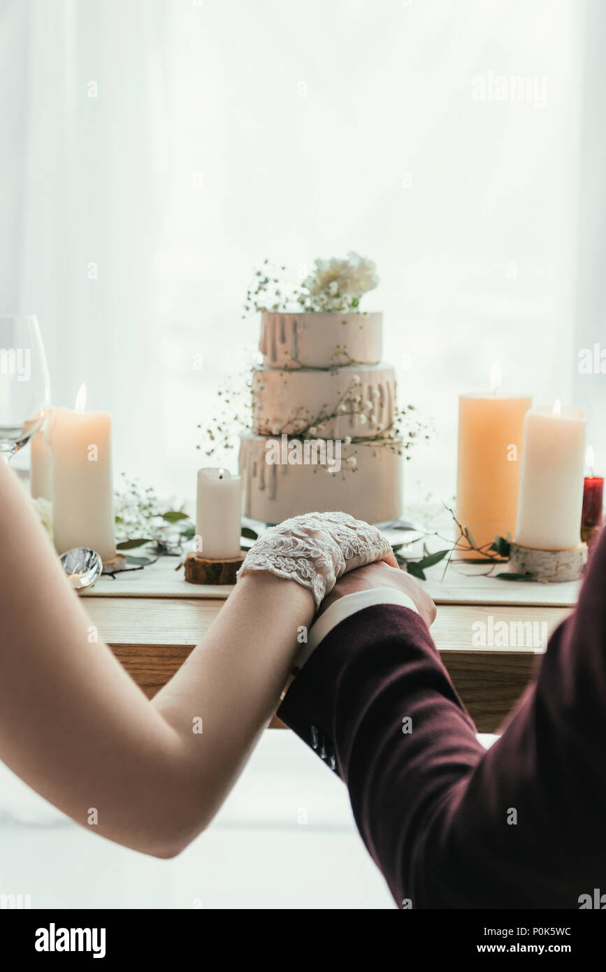 partial view of newlyweds holding hands while sitting at served table ...