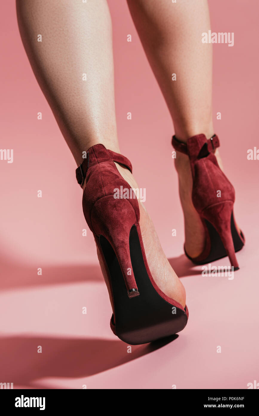 low angle view of woman feet in stylish high heeled sandals on pink ...