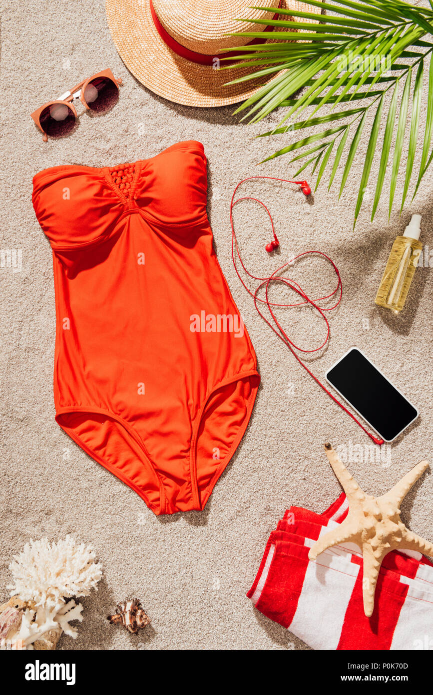 top view of stylish red swimsuit with smartphone and accessories lying ...