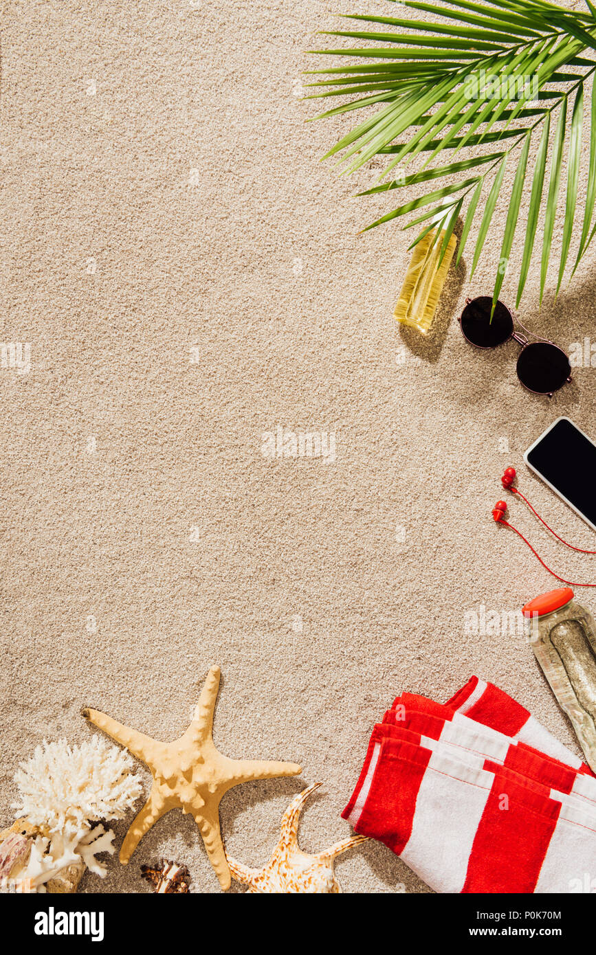 top view of striped towel with various objects lying on sandy beach ...