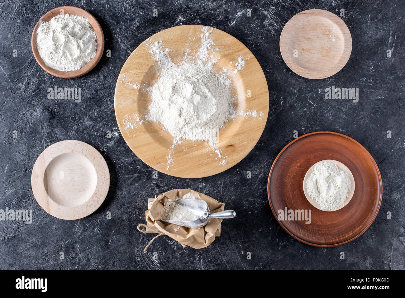 flat lay with arrangement of wooden plates and flour on dark marble ...