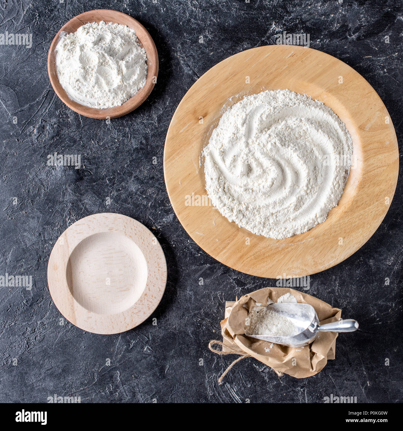flat lay with arrangement of wooden plates and flour on dark marble ...