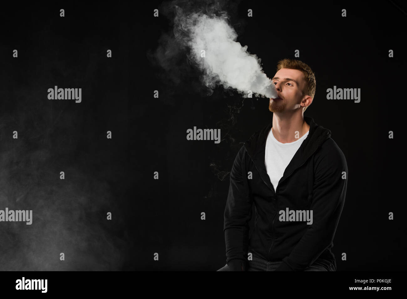 Young bearded man vaping electronic cigarette surrounded by clouds of ...