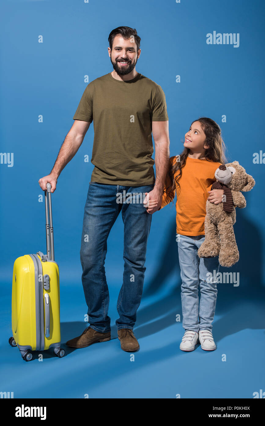 father and daughter standing with yellow travel bag and teddy bear on ...