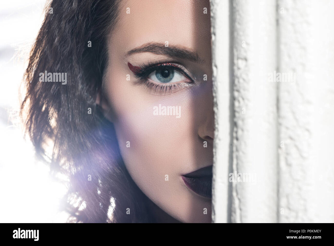 cropped image of beautiful girl standing behind column and looking at ...
