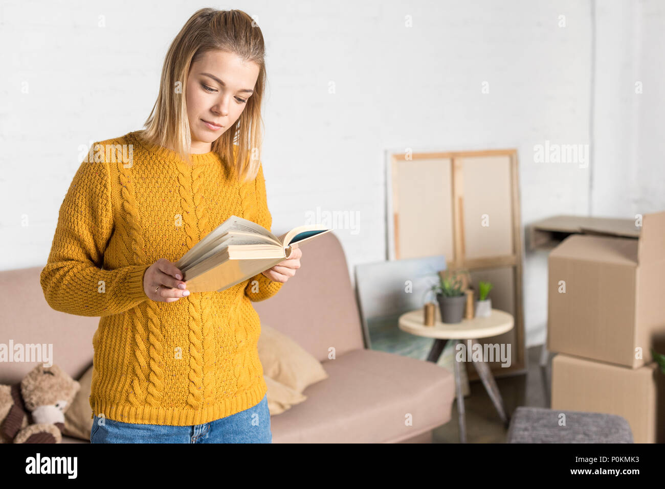 attractive young woman reading book while moving home Stock Photo - Alamy