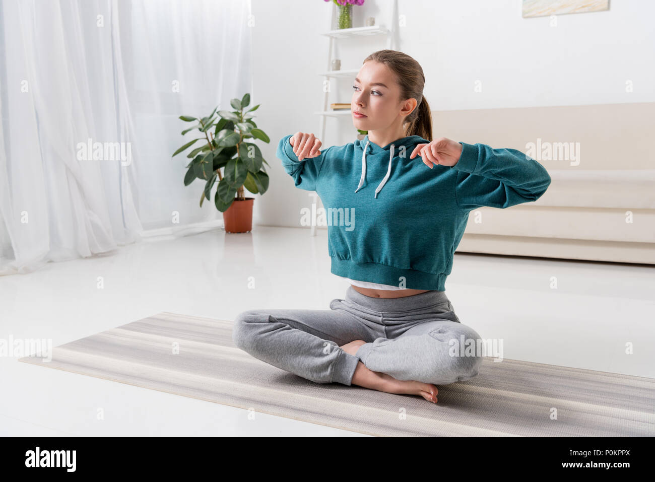 girl sitting in lotus position and stretching on yoga mat at home Stock ...