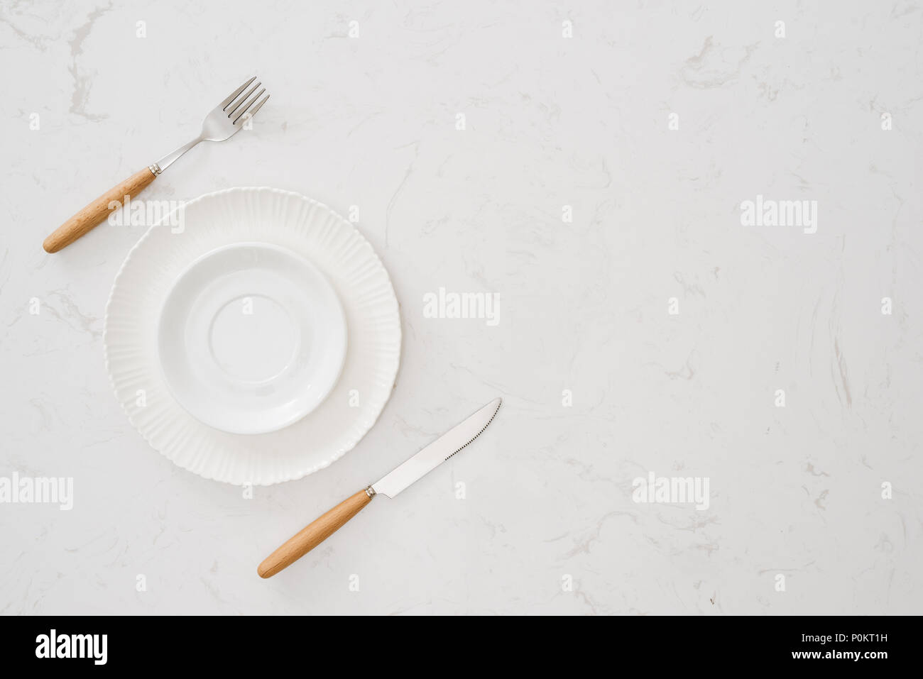 Eating concept. Spoon, fork and white dish on white stone background ...