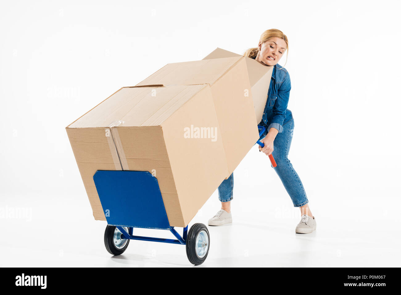 Attractive woman trying to push delivery cart with boxes isolated on ...