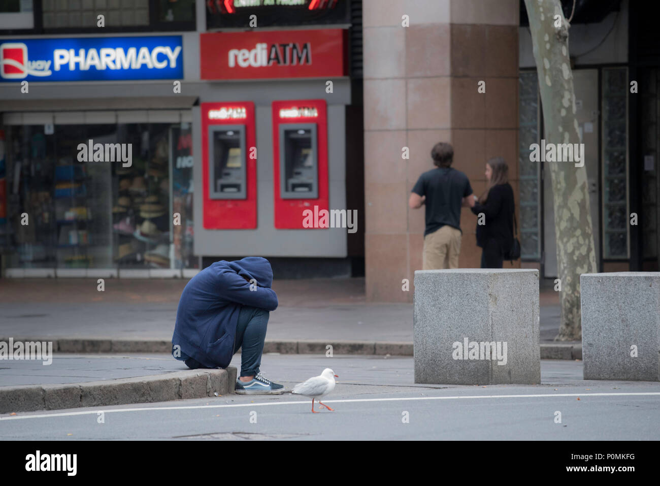 A person alone and sitting on a footpath edge with their head down and ...