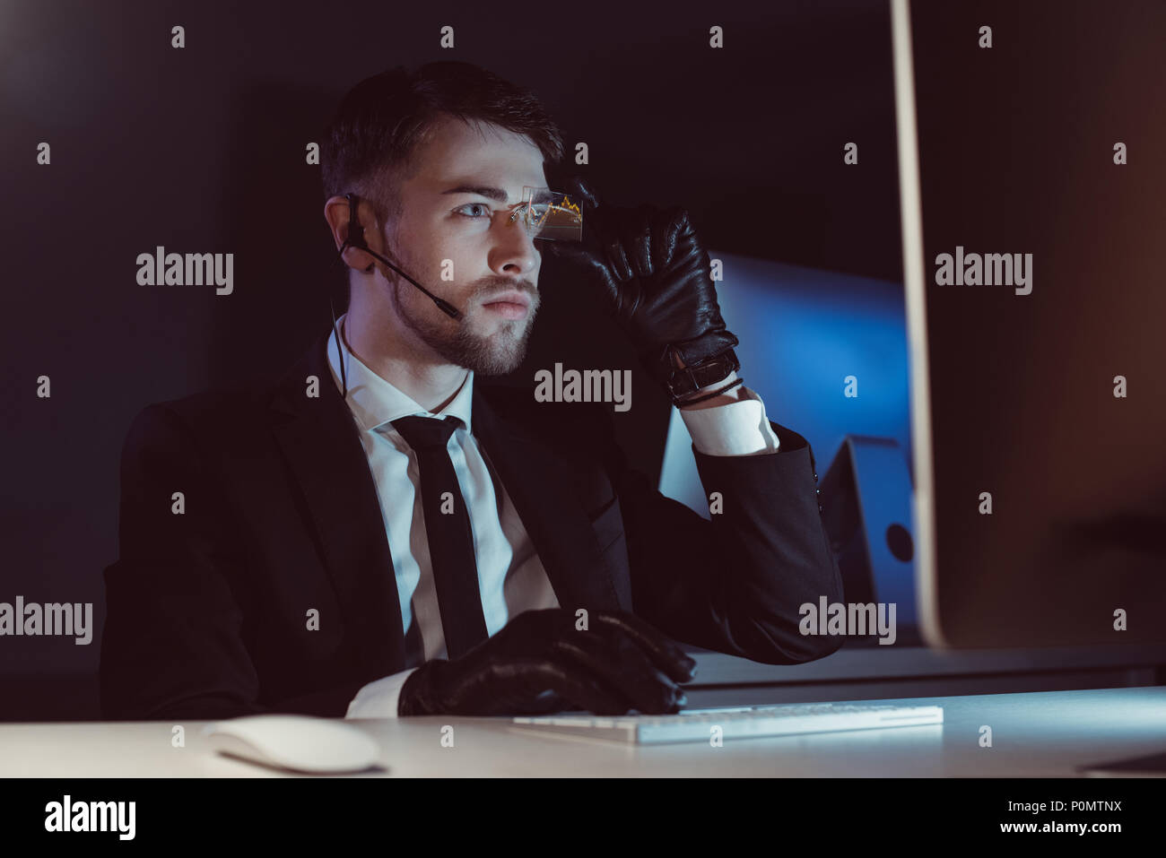 portrait of spy agent with headset looking at computer screen at table ...