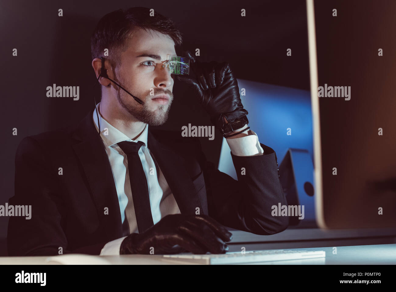 portrait of hacker with headset looking at computer screen at table in ...