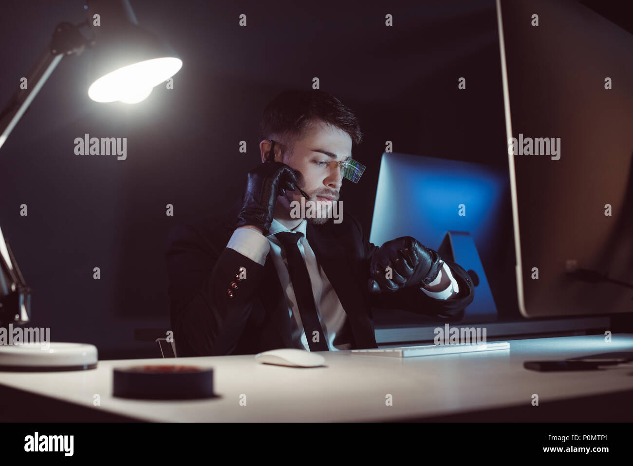 portrait of spy agent in gloves with headset checking time at table ...