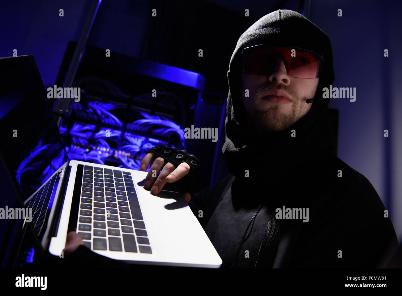 side view of hacker in eyeglasses with laptop looking away with cables ...