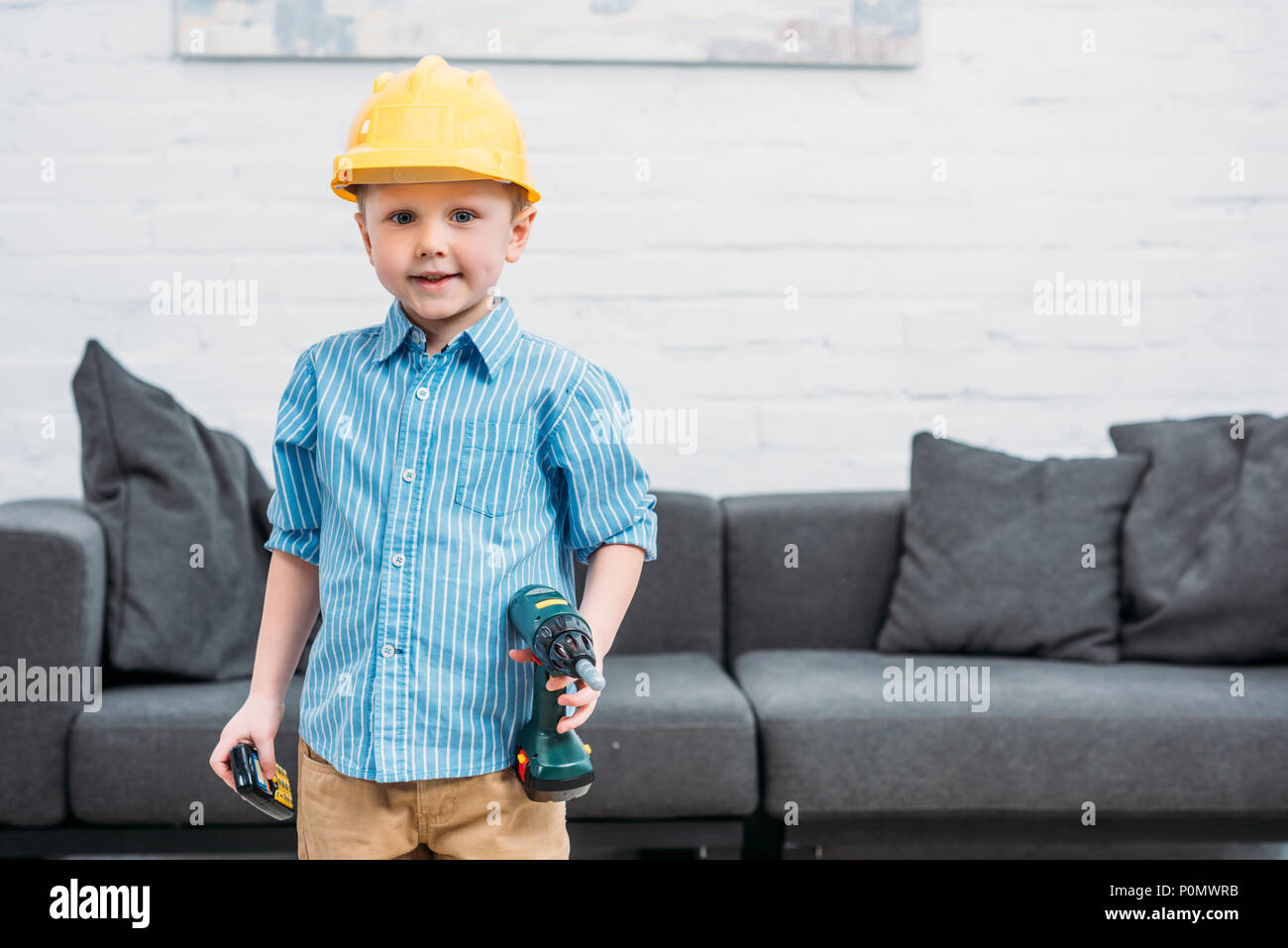 Little boy in safety helmet with toy drill pretending to be workman ...