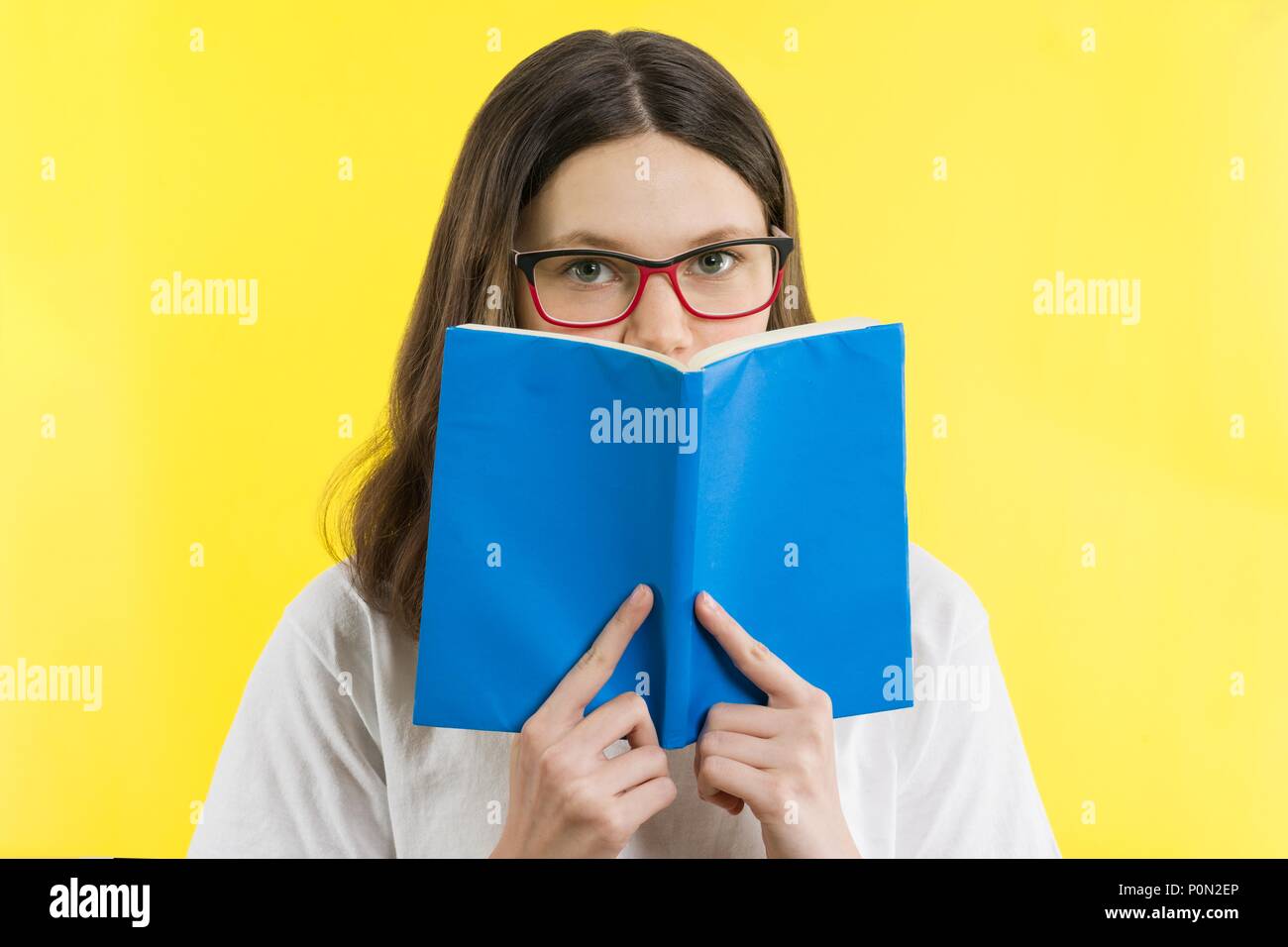 Closeup portrait teenage girl with eye glasses looking over a book ...