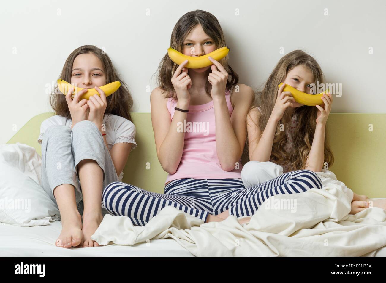 Sisters of children in pajamas play in the morning in bed. Use bananas ...