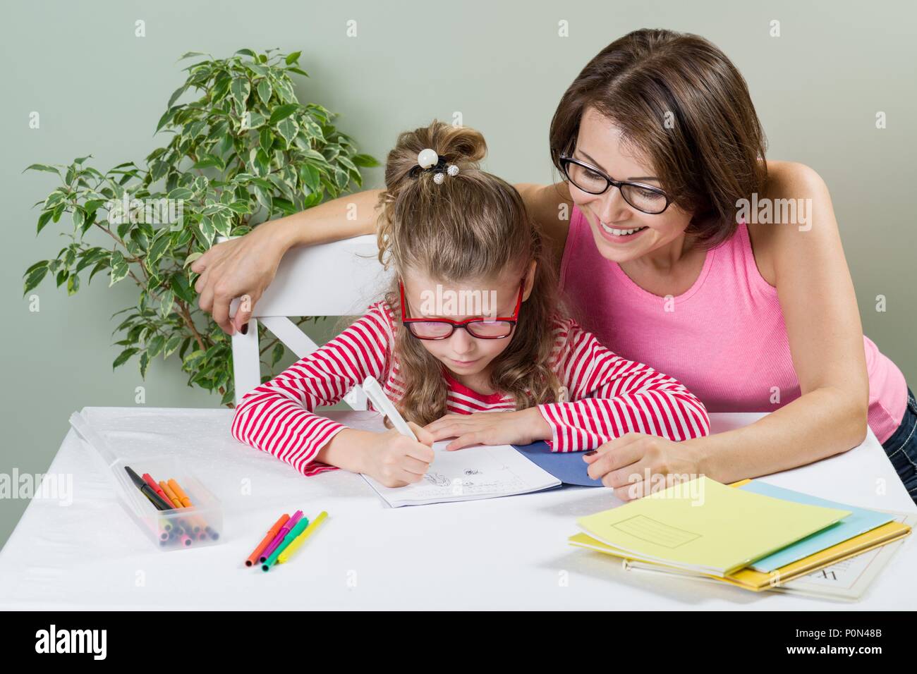 Loving mother helping her daughter elementary school pupil write in her ...