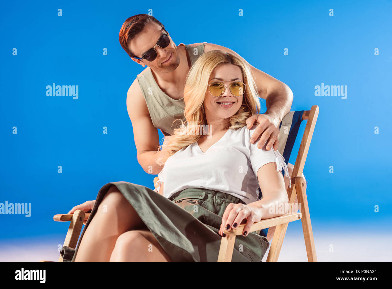 Man hugging woman sitting in deck chair on blue background Stock Photo ...