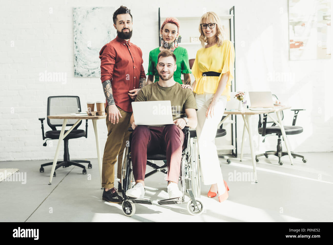 smiling disabled businessman with laptop and colleagues standing behind ...