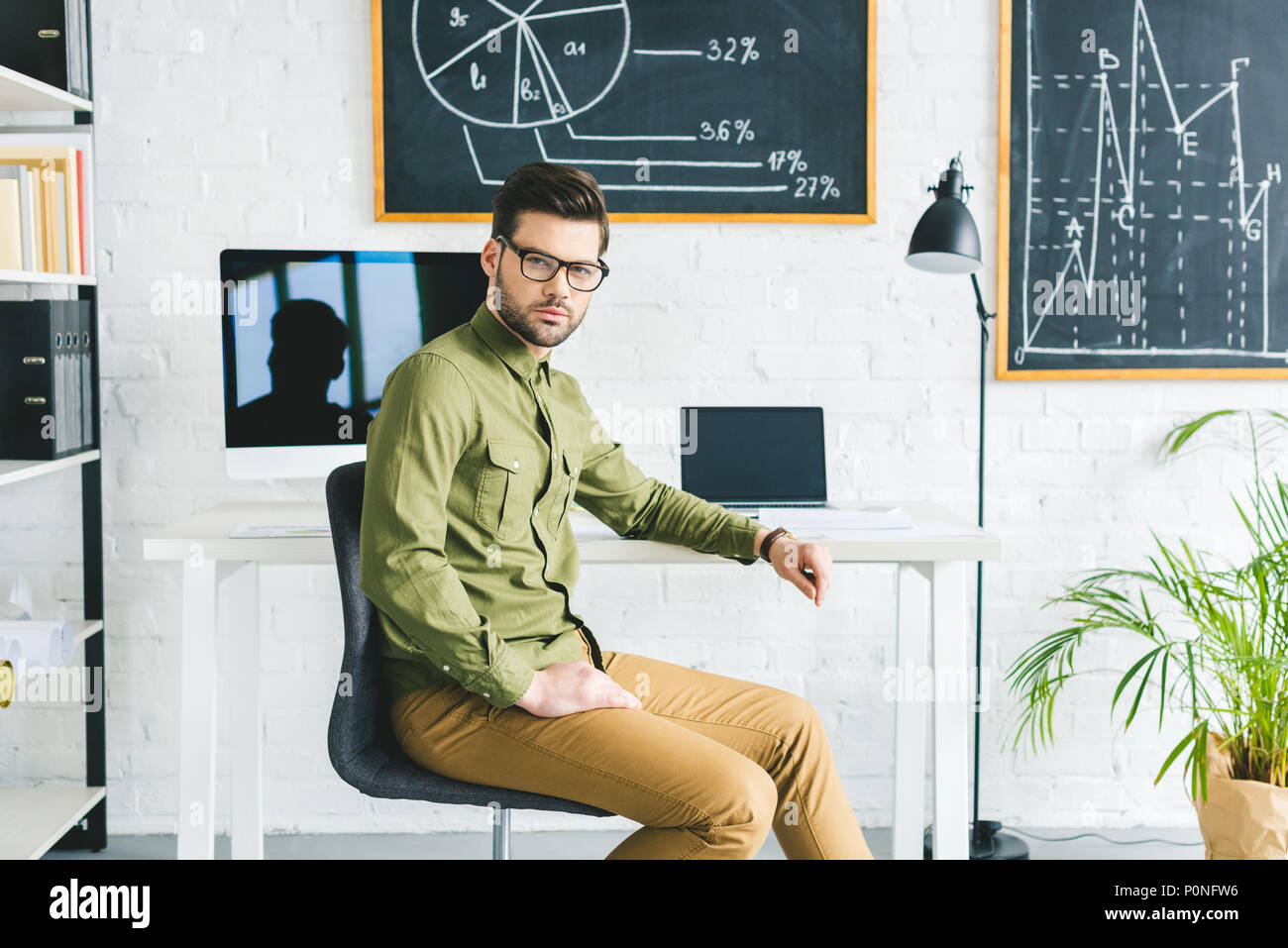 Serious man sitting by table with computers in light office Stock Photo ...