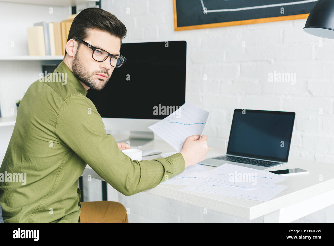 Thoughtful young man by working table with computers at home office ...