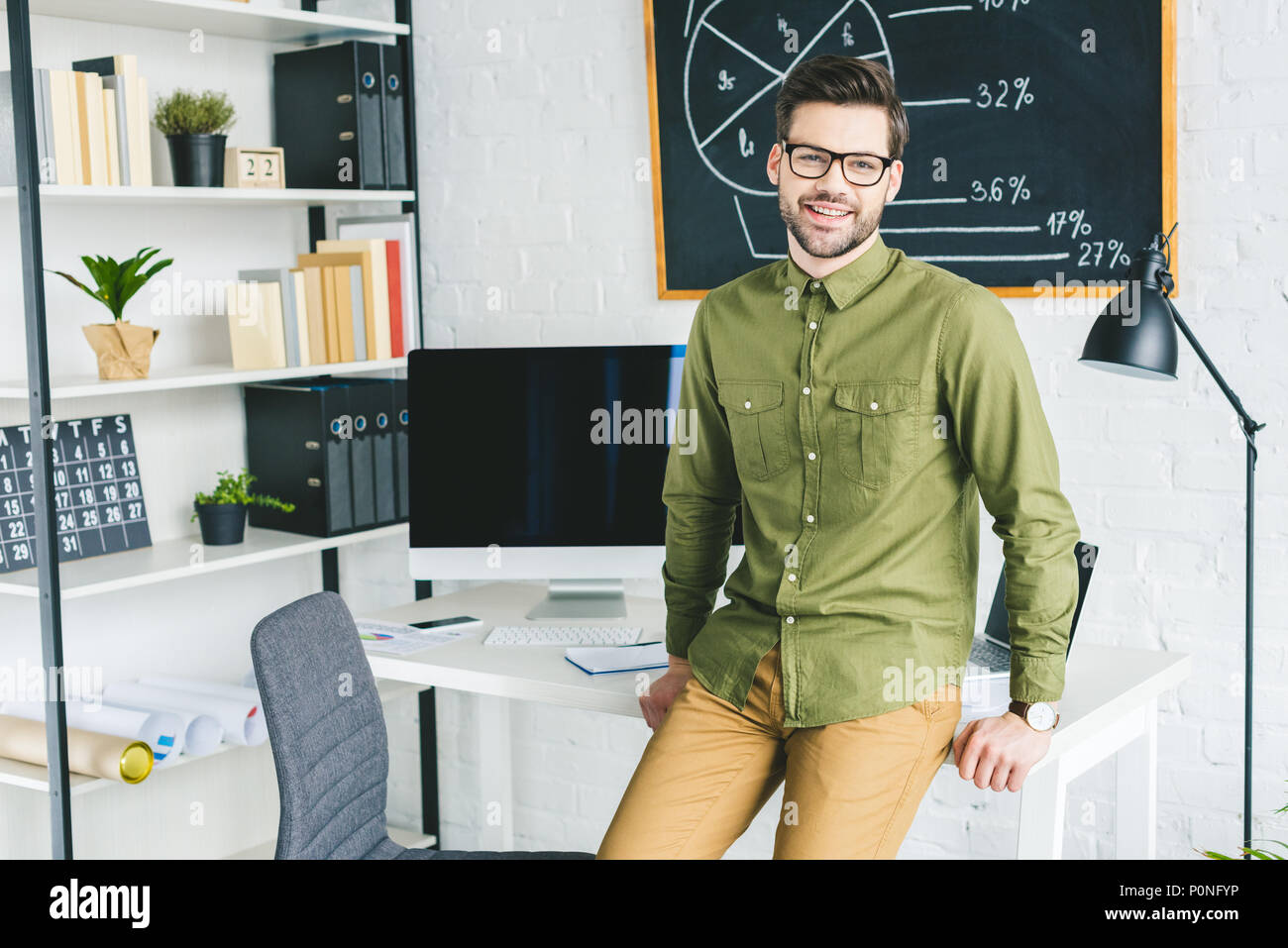 Handsome man standing by table with computer in light office Stock ...