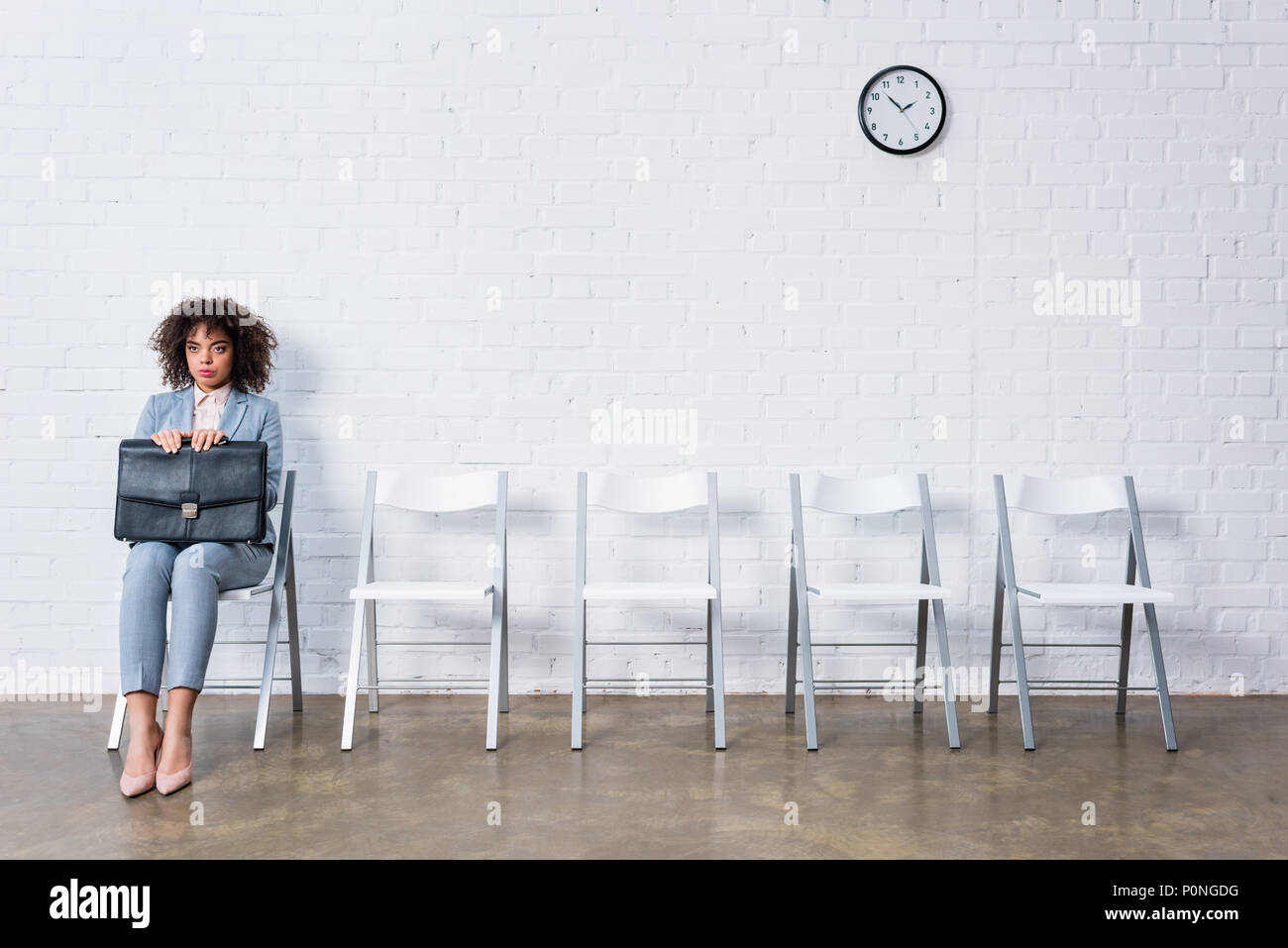 Confident businesswoman with briefcase sitting on chair and waiting ...