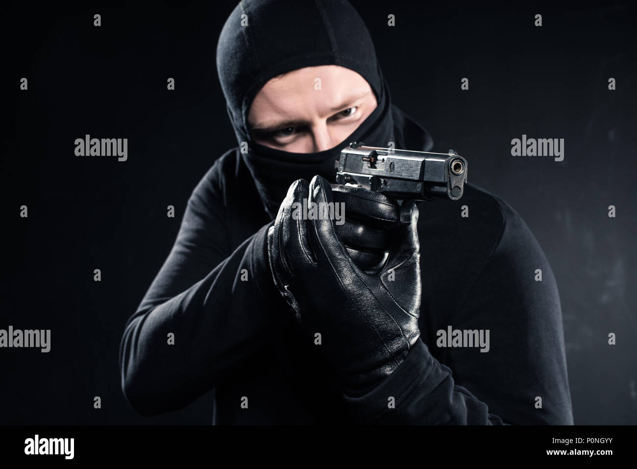 Male robber in balaclava aiming with gun on black Stock Photo - Alamy
