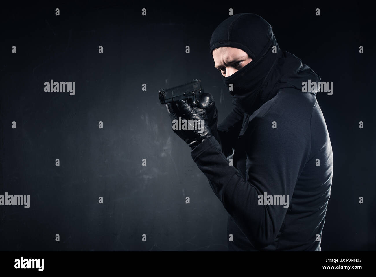 Male criminal in balaclava and gloves aiming with gun on black Stock ...