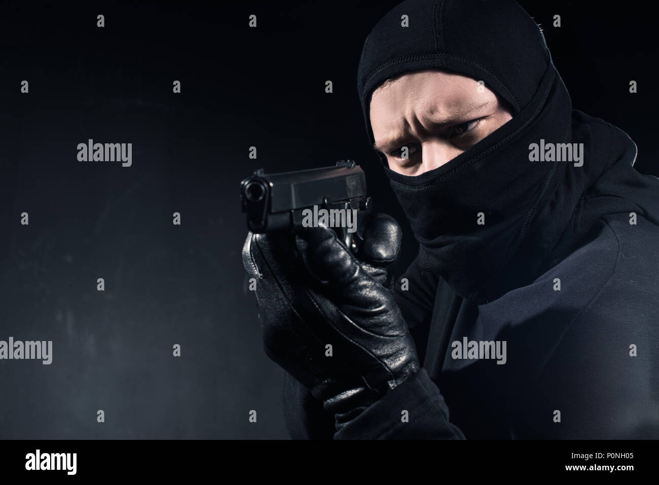Robber in balaclava and gloves aiming with gun on black Stock Photo - Alamy