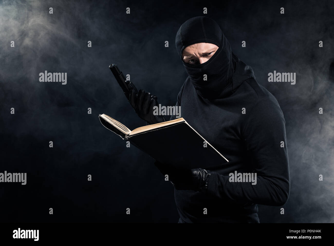 Man in black balaclava holding gun and reading book Stock Photo - Alamy