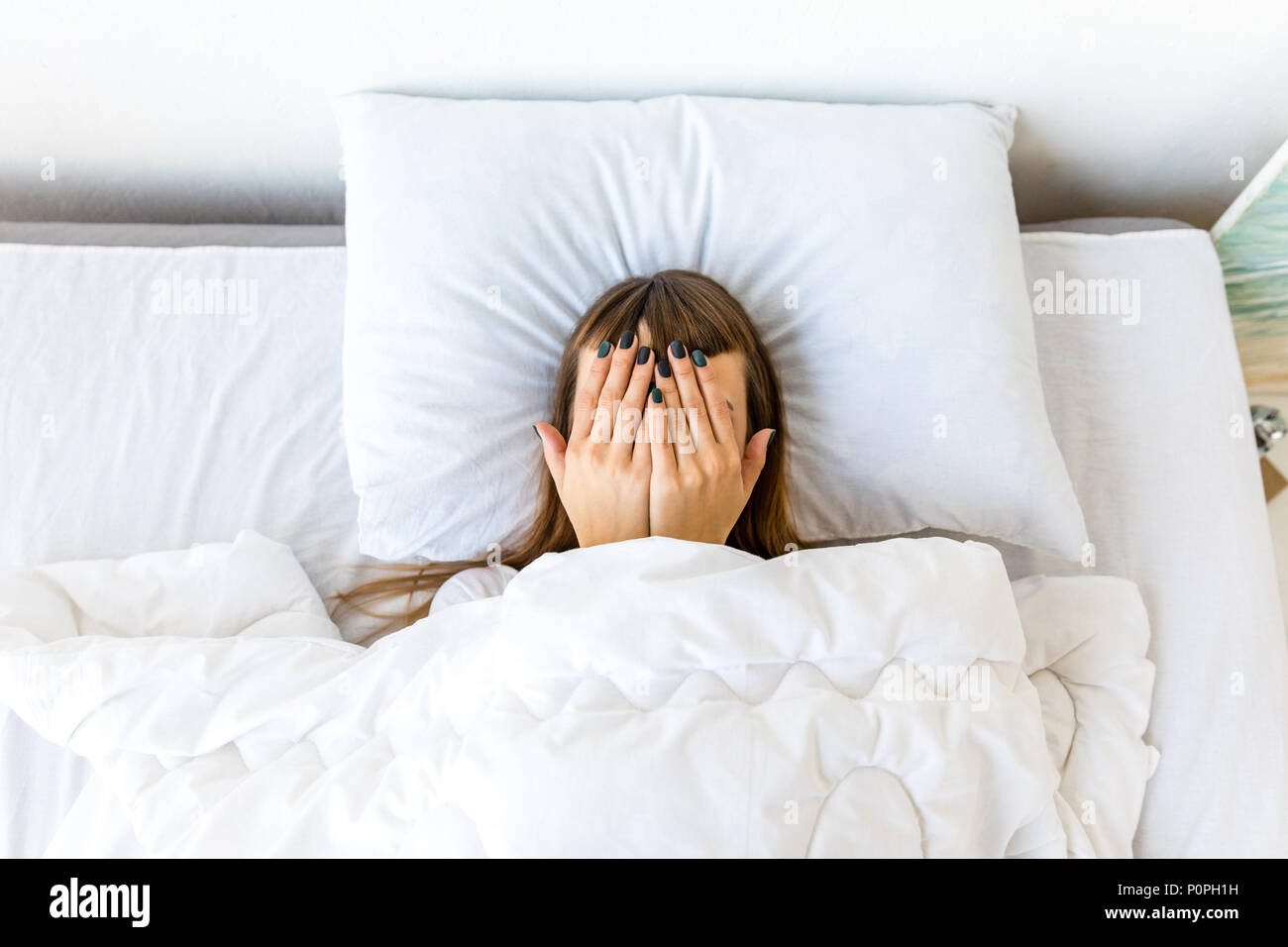 obscured view of woman covering face with hands while lying in bed ...