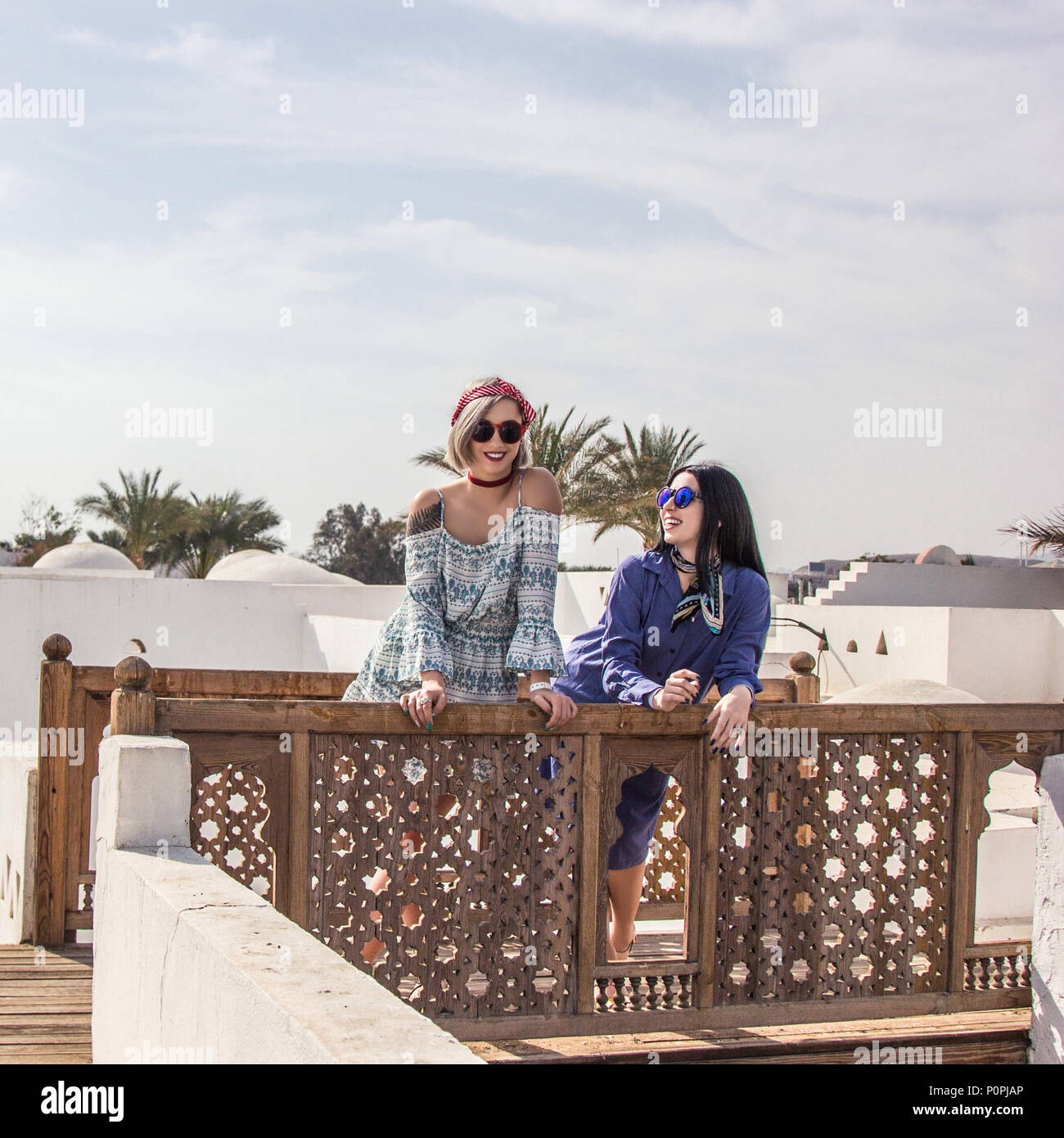 beautiful smiling girls in dresses and sunglasses leaning at wooden ...
