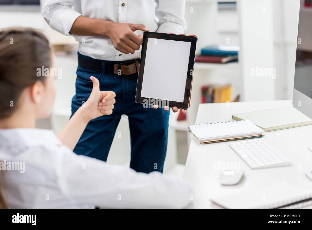 partial view of girl showing thumb up to classmate with tablet in hands ...