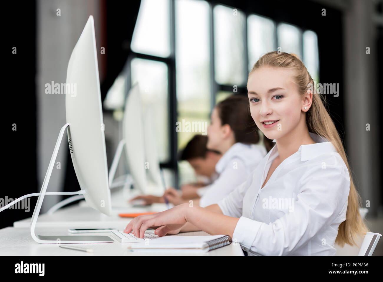 side view of smiling teen girl looking at camera while working on ...