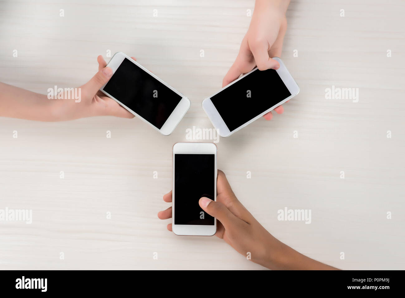 cropped shot of teenagers holding smartphones with blank screens in ...