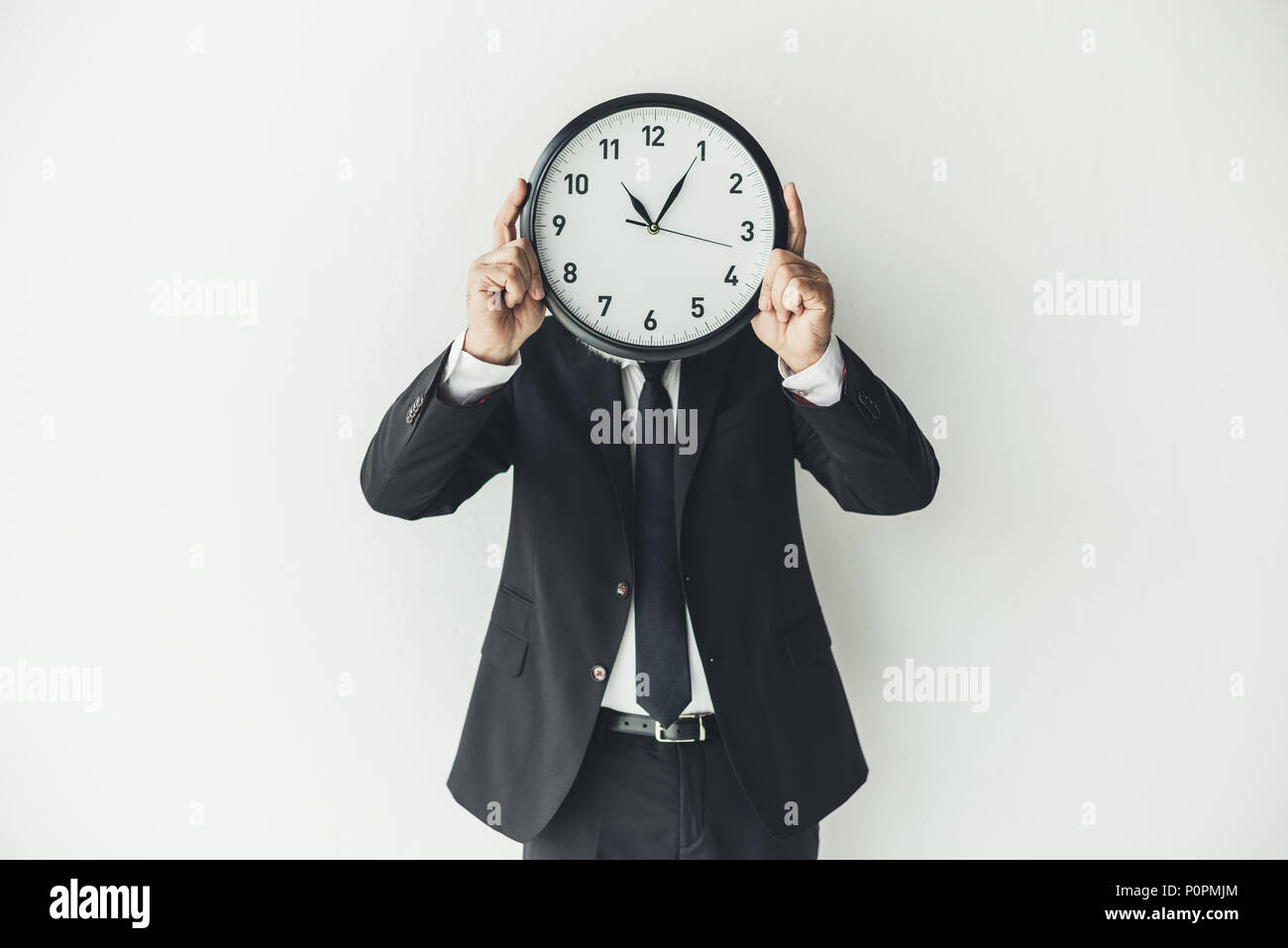man covering face with clock on light background Stock Photo - Alamy