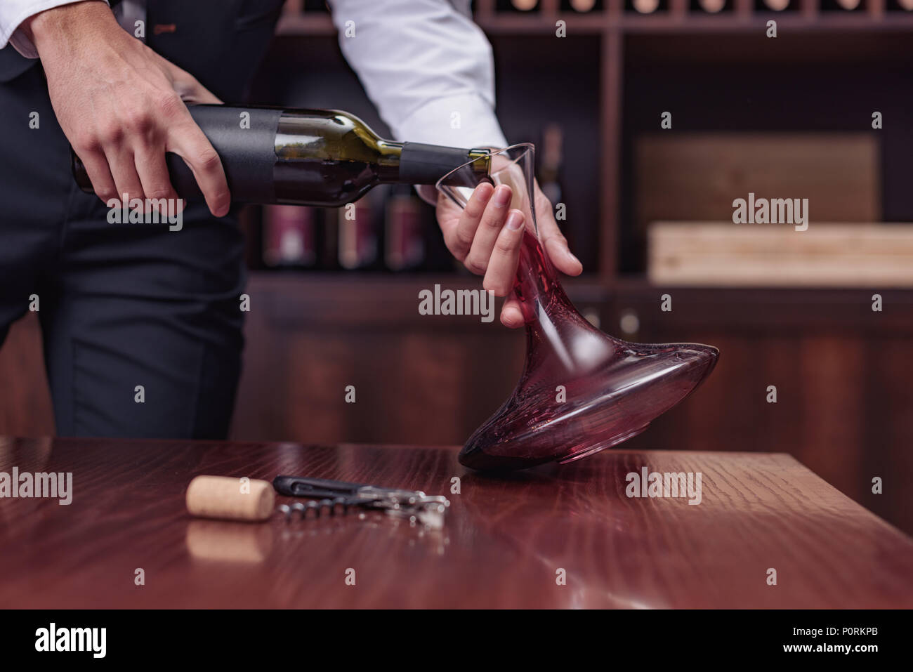Cropped view sommelier pouring red wine from bottle into decanter at ...
