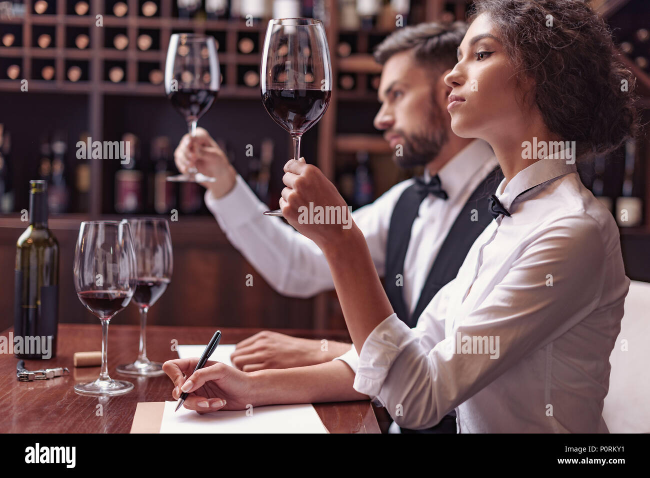 Two sommeliers, male and female tasting red wine and making notes at ...