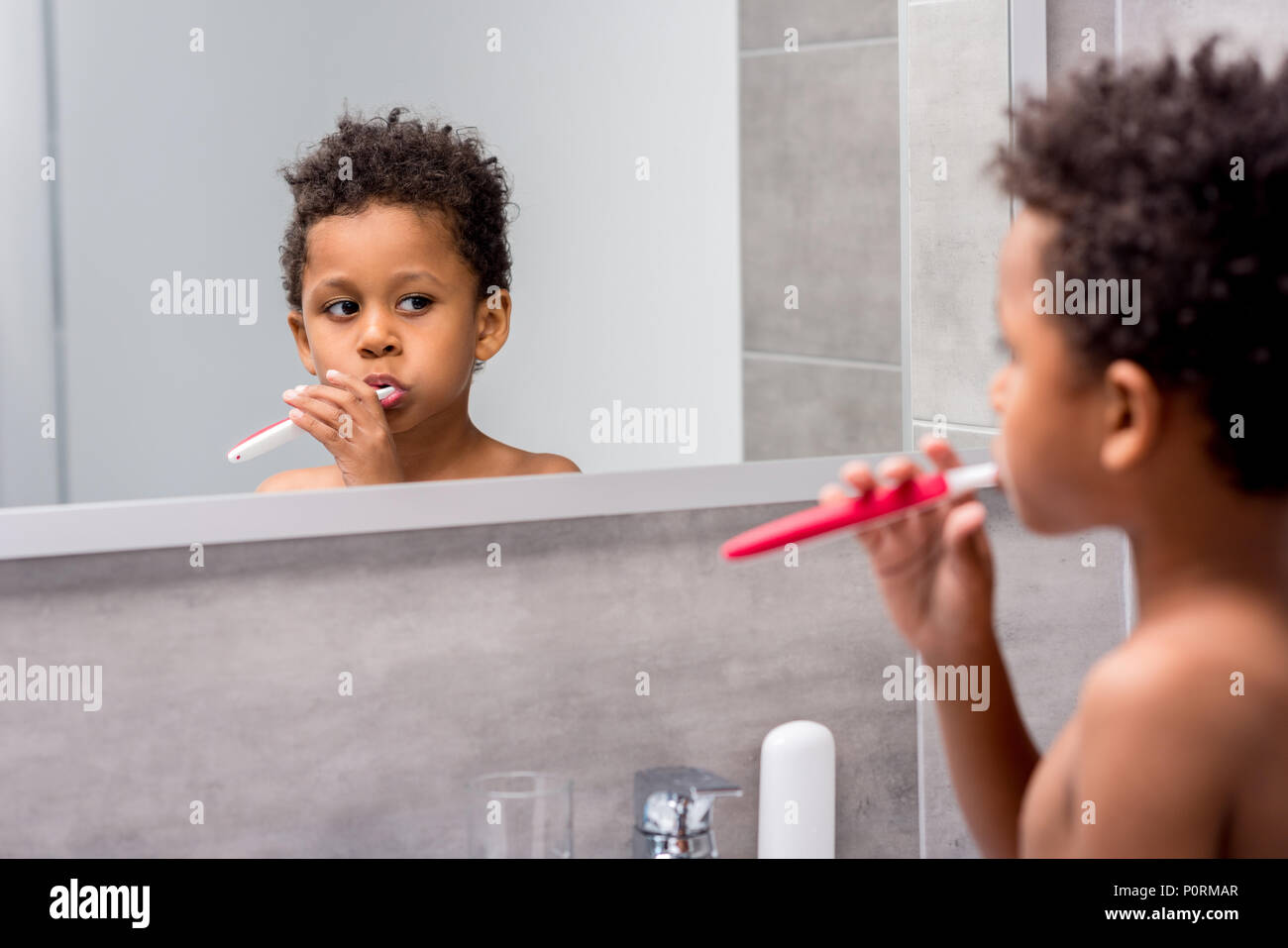 beautiful african-american kid brushing teeth while looking at mirror ...