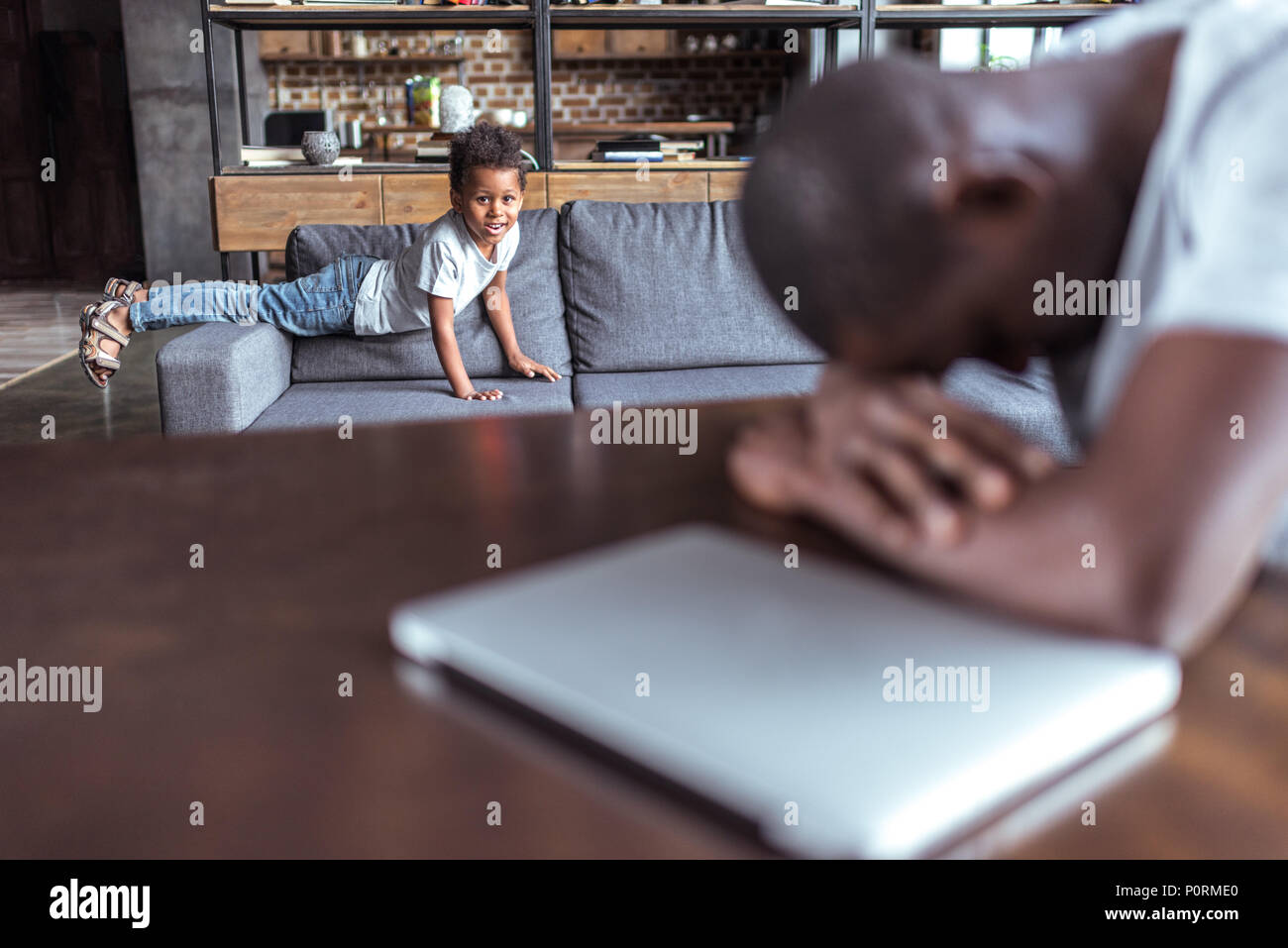 boy playing while overworked father sleeping on table with laptop Stock ...